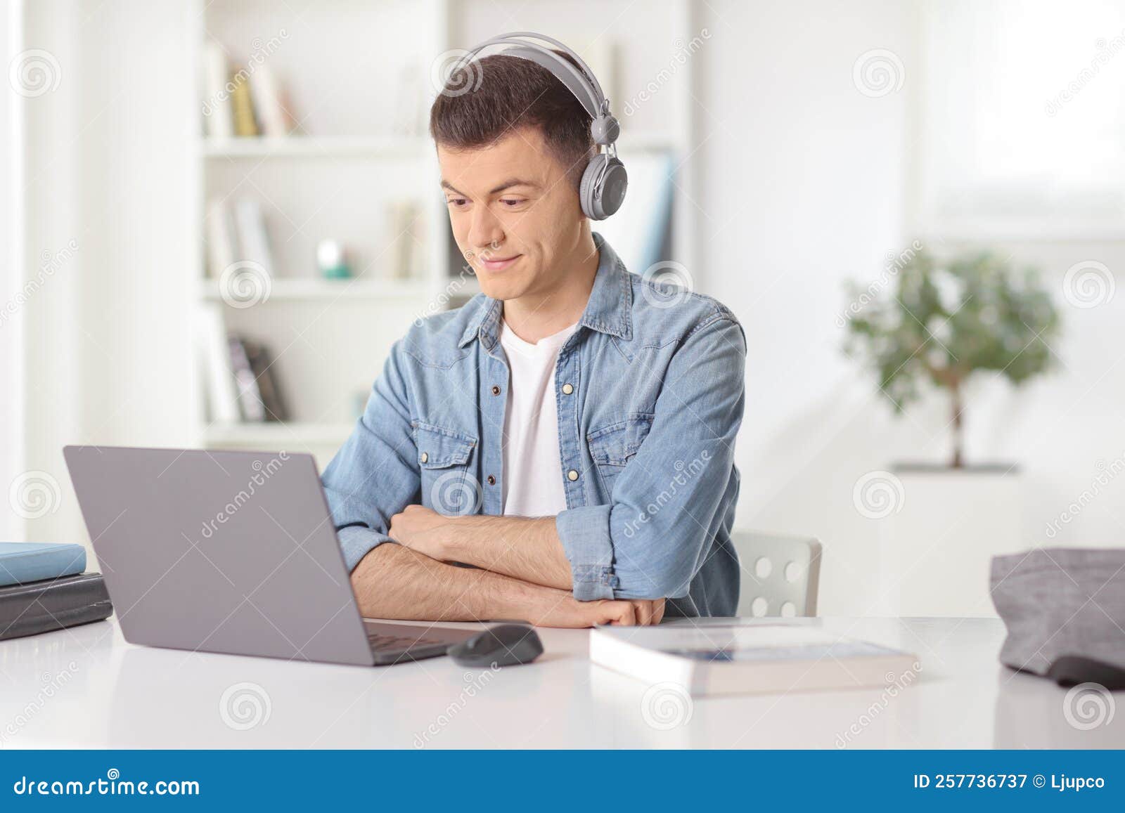 Young Man Sitting in Front of a Laptop at Home and Listening a Tutorial ...