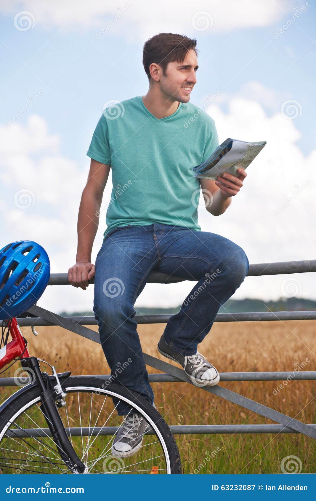 Young Man Sitting on Gate and Reading Map on Bike Ride Stock Image ...