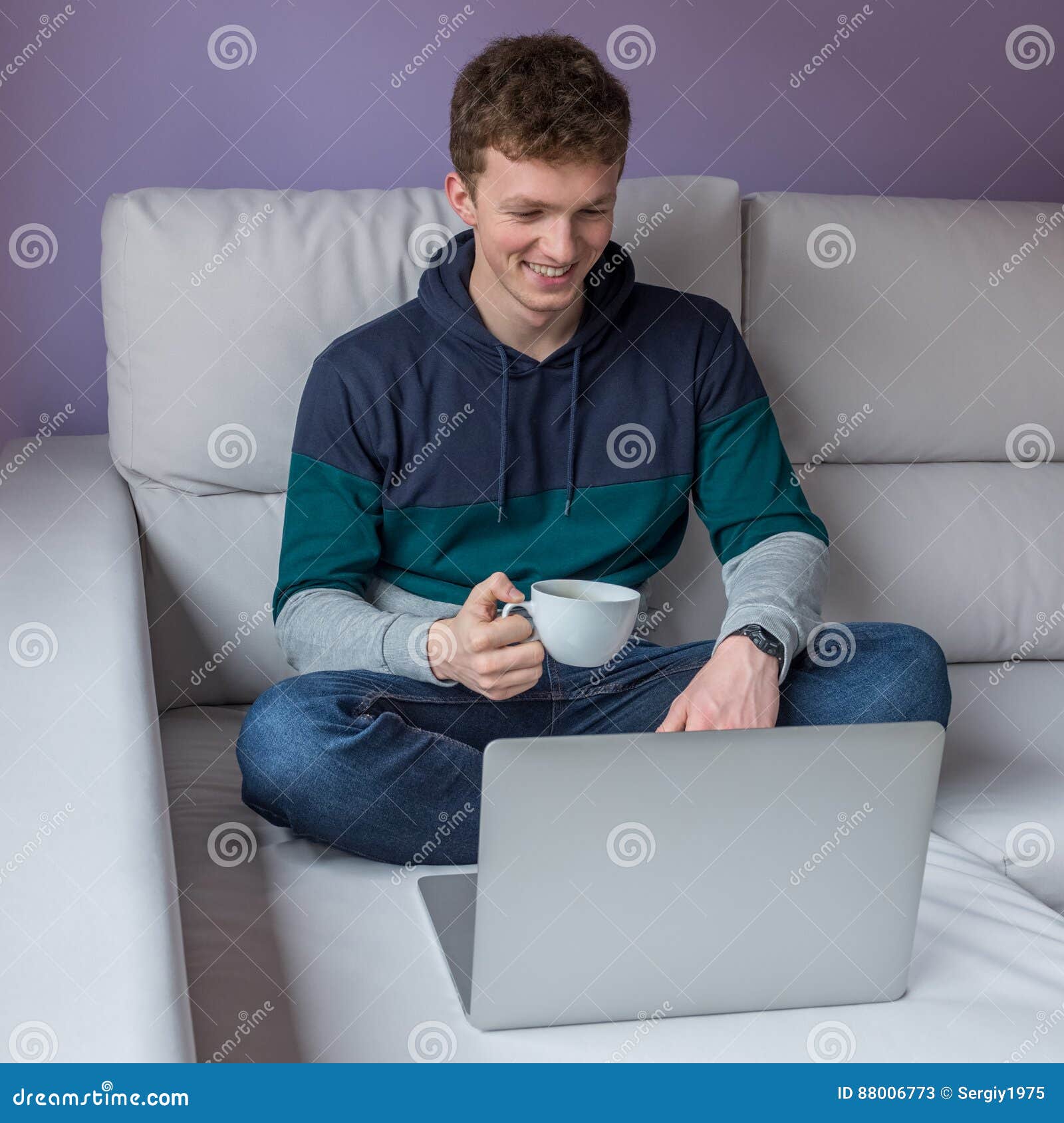 Young Man Sitting on the Sofa with a Cup of Coffee in Front of Laptop ...