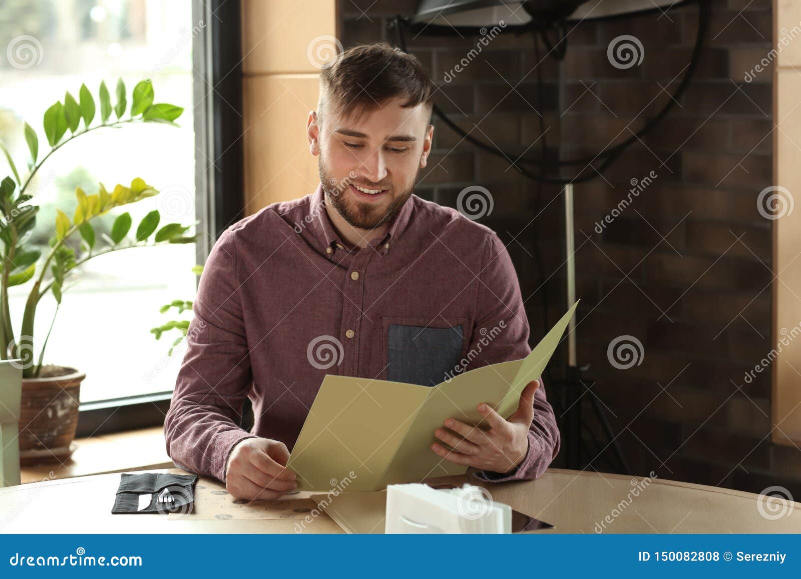 Young Man Sitting at Table while Reading Menu in Restaurant Stock Photo ...