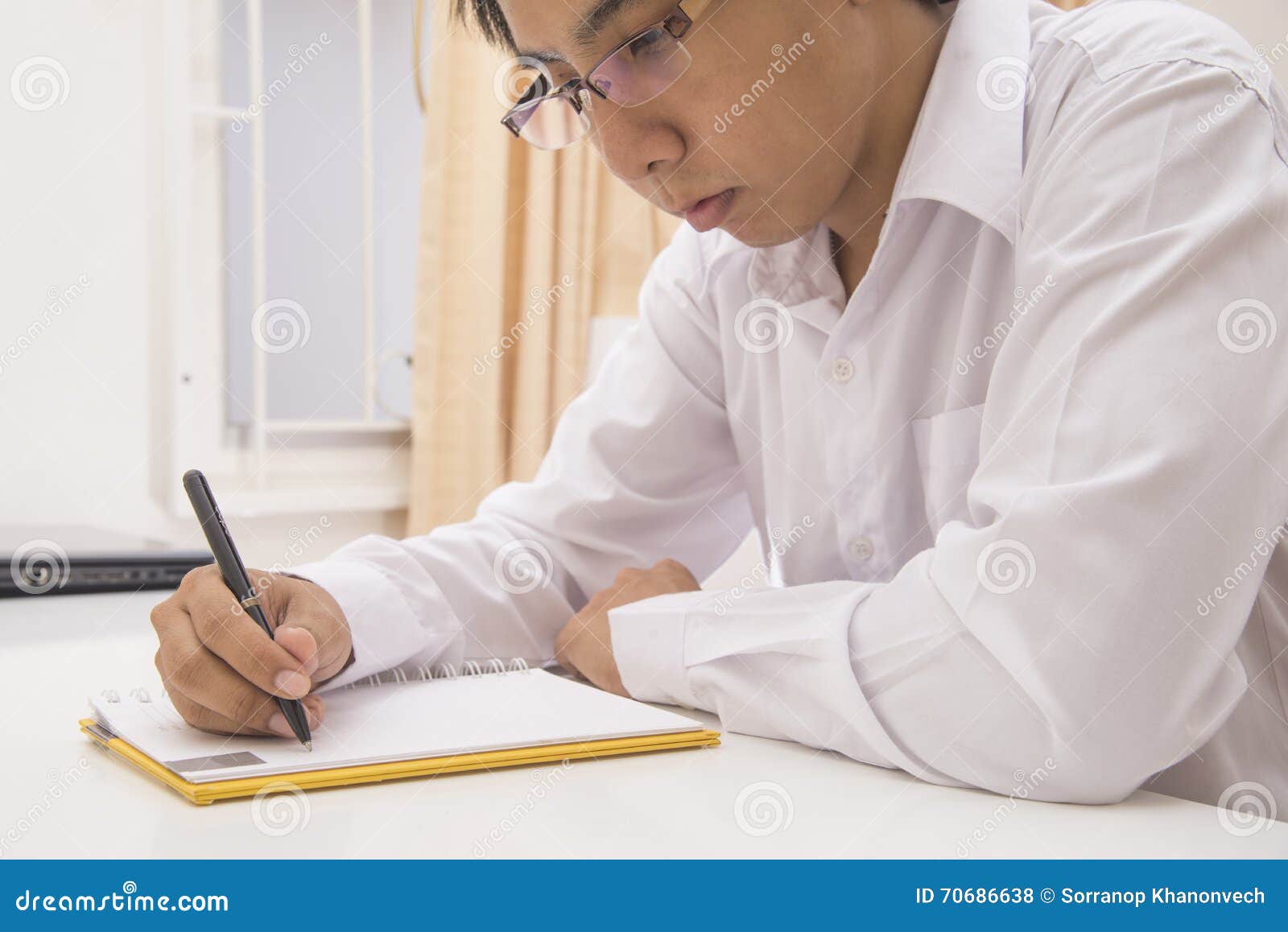 A Young Man is Sitting at a Table and is Writing in a Notebook. Stock ...