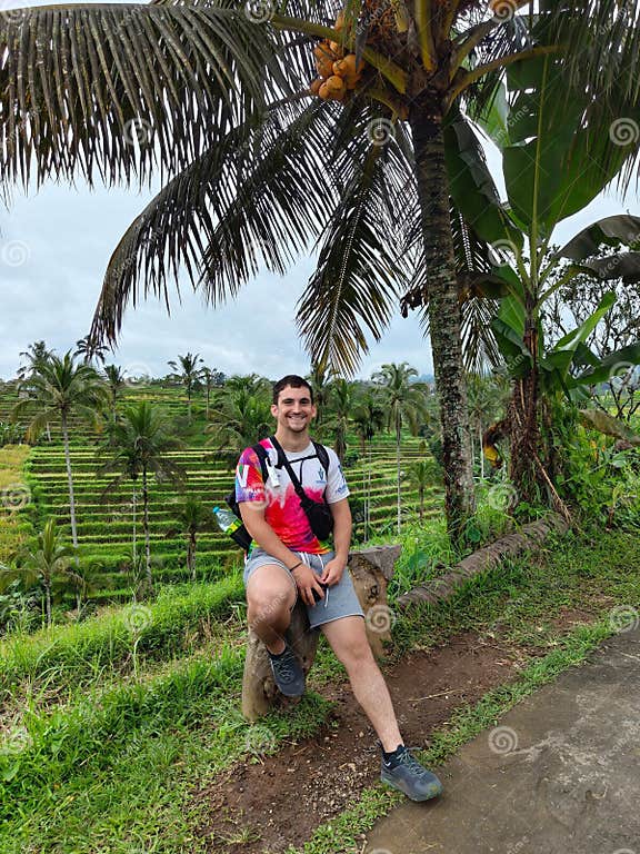 Young Man Sitting on a Tree Stump with Lush Greenery and Fields Behind ...