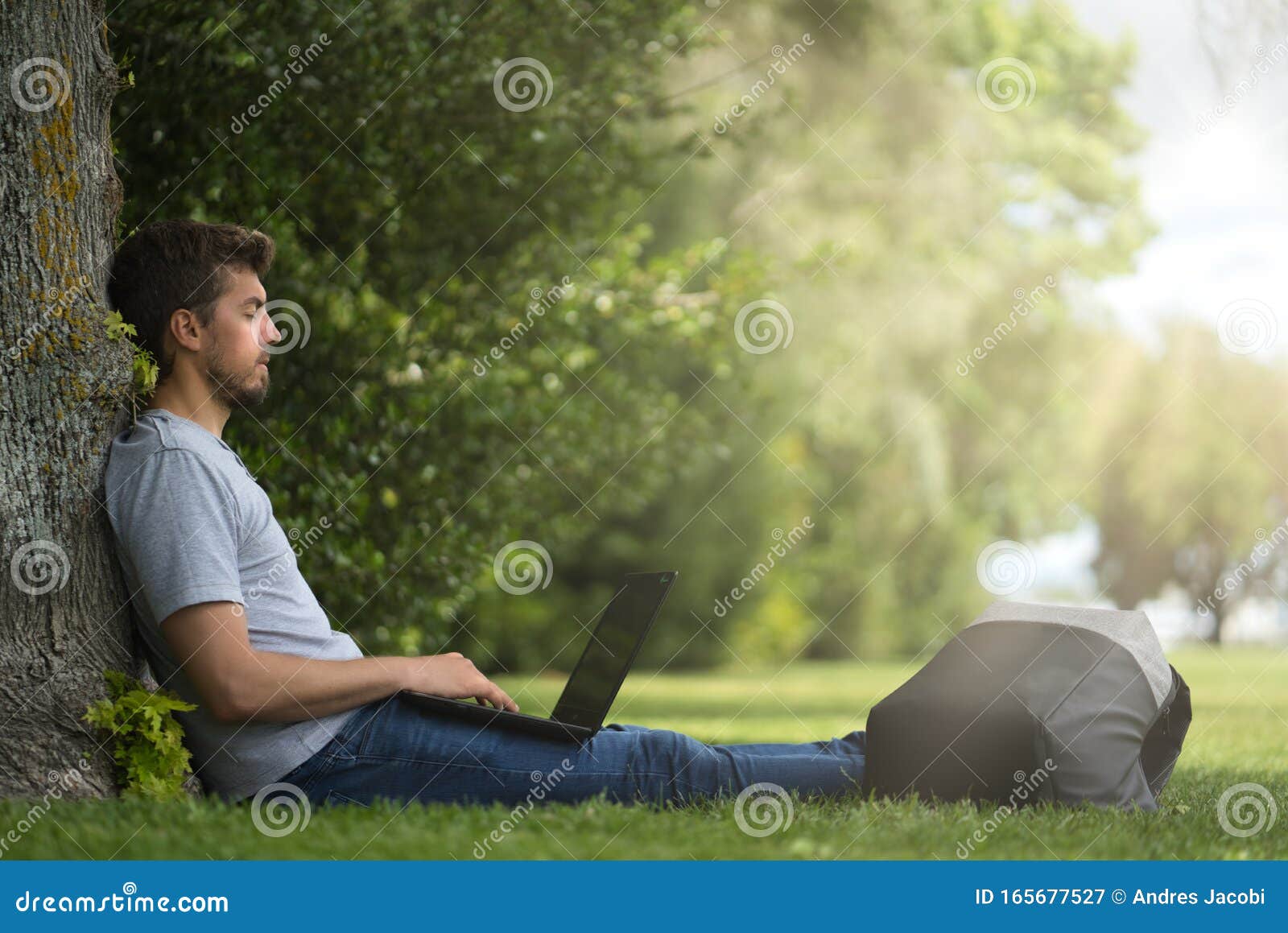 Young Man Sitting Under a Tree with His Legs Stretched and His Computer ...