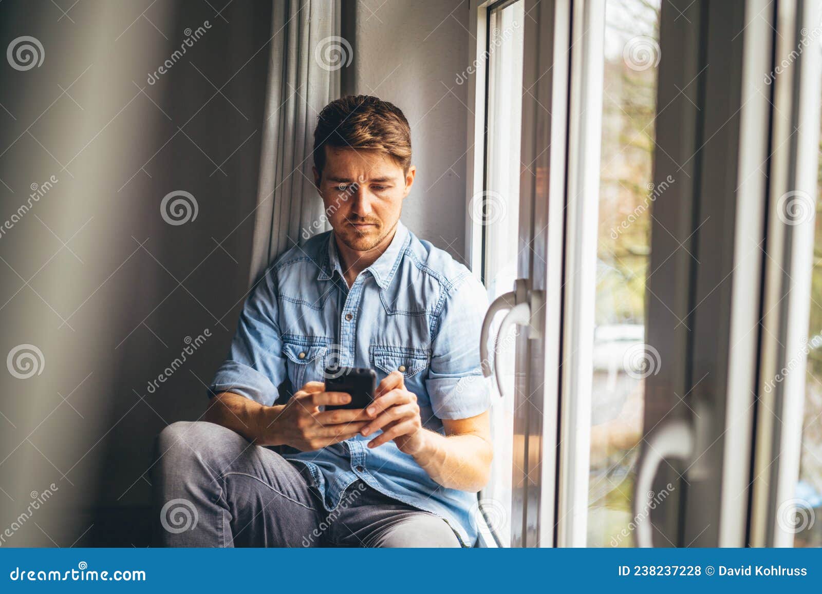 Young Man Sitting at Window and Using Smartphone Stock Photo - Image of ...
