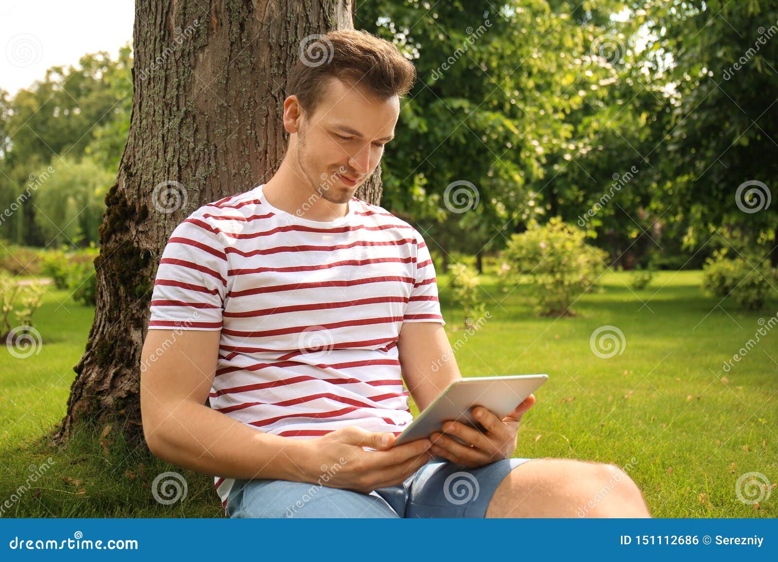 Young Man with Tablet PC Sitting Near Tree in Park Stock Photo - Image ...