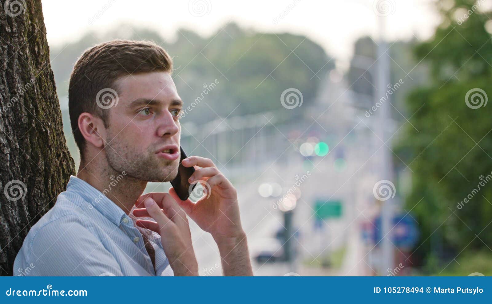 A Young Man Talking on the Phone Under a Tree Stock Photo - Image of ...