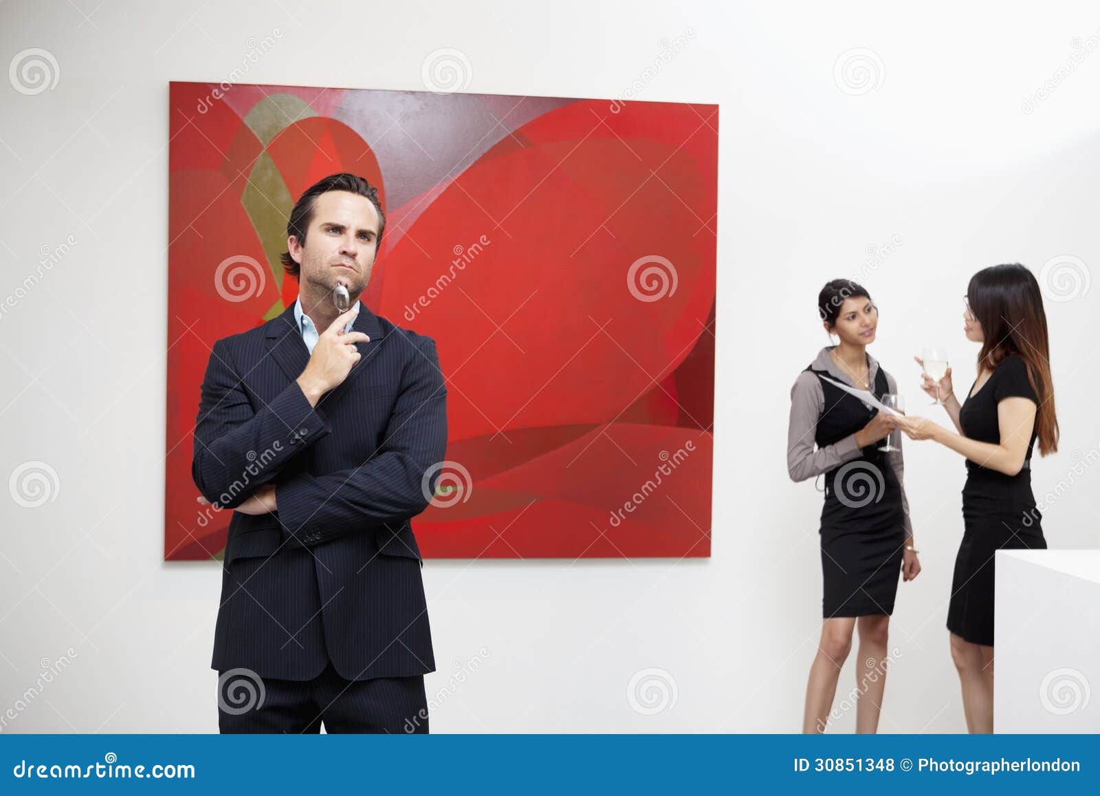Young Man Thinking with Two Women Talking in Background in Art Gallery ...