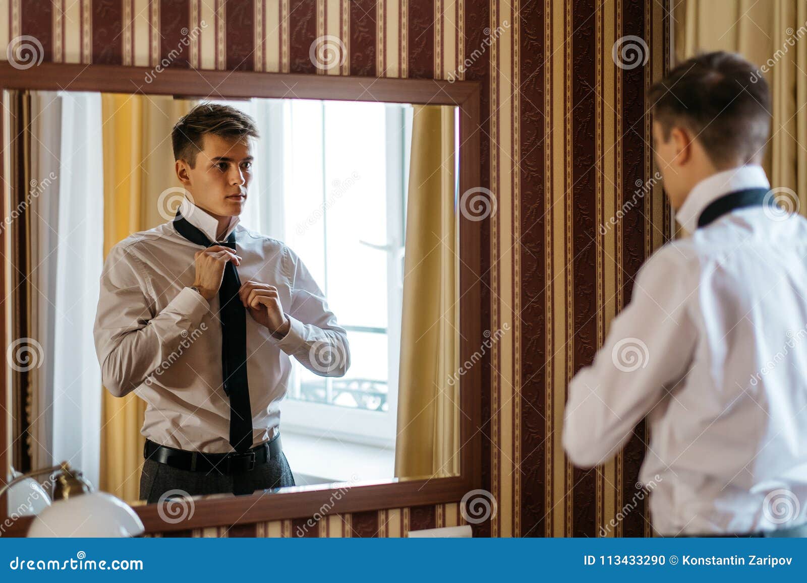 A Young Handsome Man Ties Up a Tie in Front of a Mirror Stock Photo ...