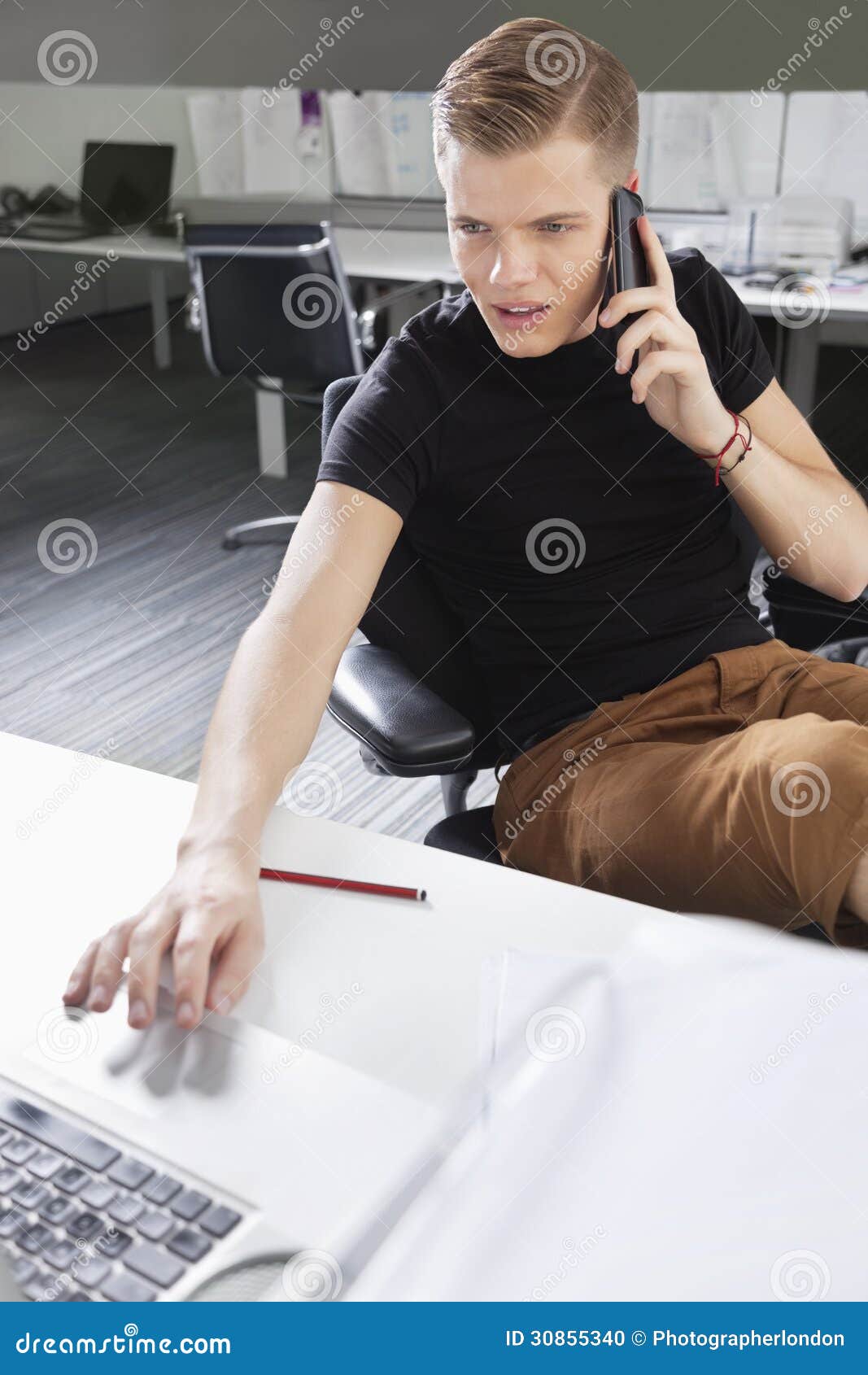 Young Man Using Cell Phone and Laptop at Desk in Office Stock Photo ...