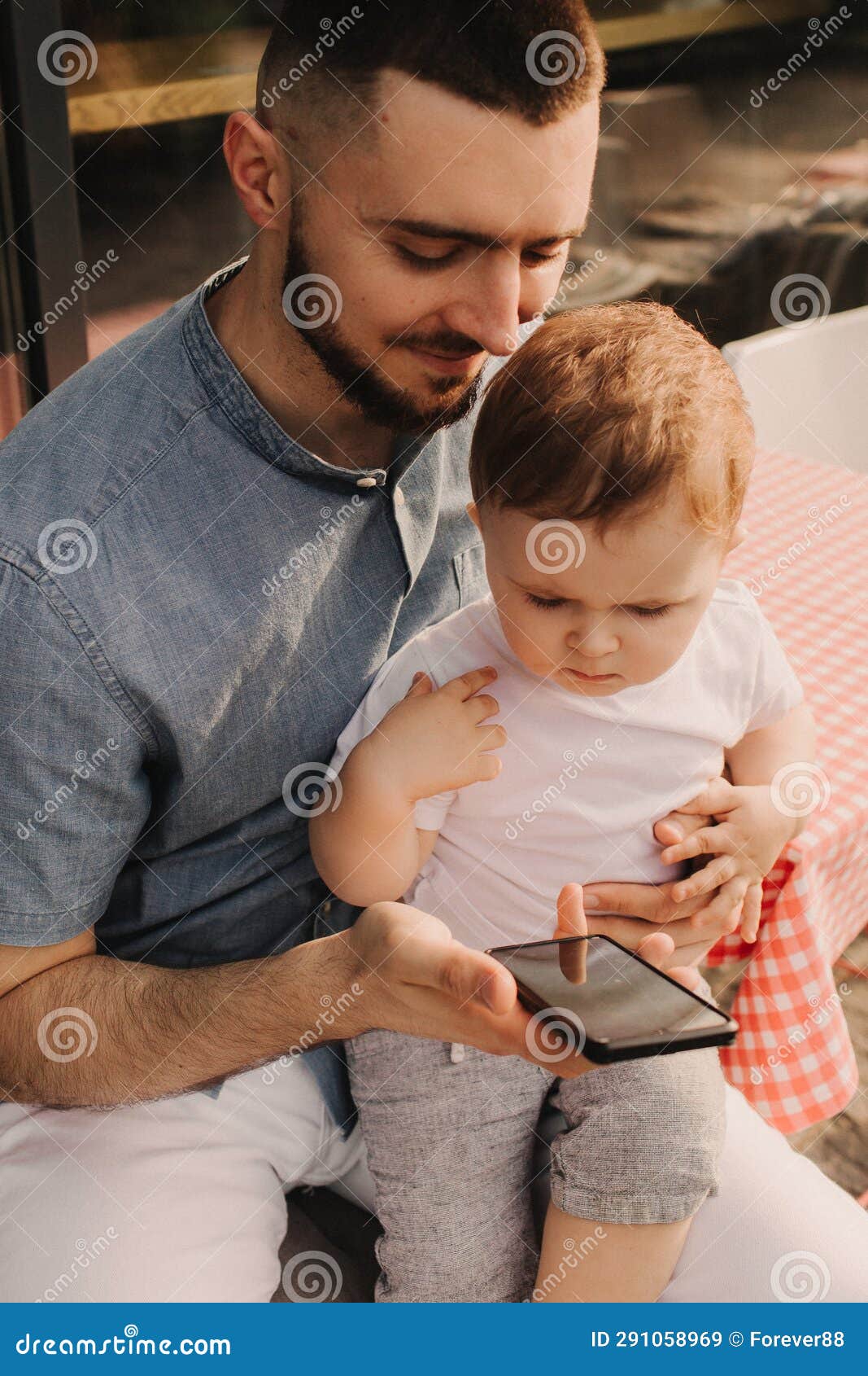 Young Man Using a Phone Mobile for Work and Holding His Son on His Hand ...