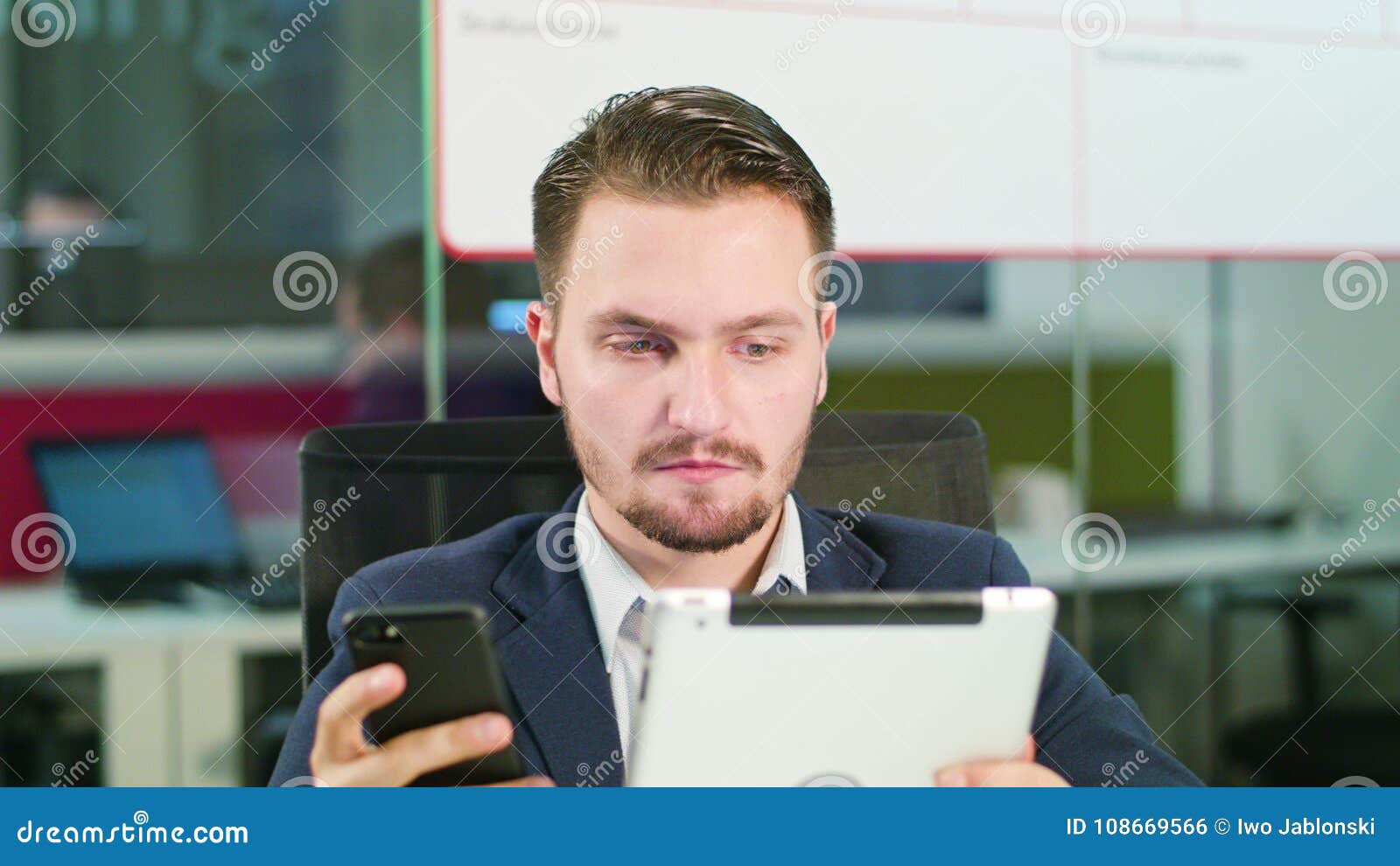 Young Man Using a Phone and a Tablet in the Office Stock Photo - Image ...