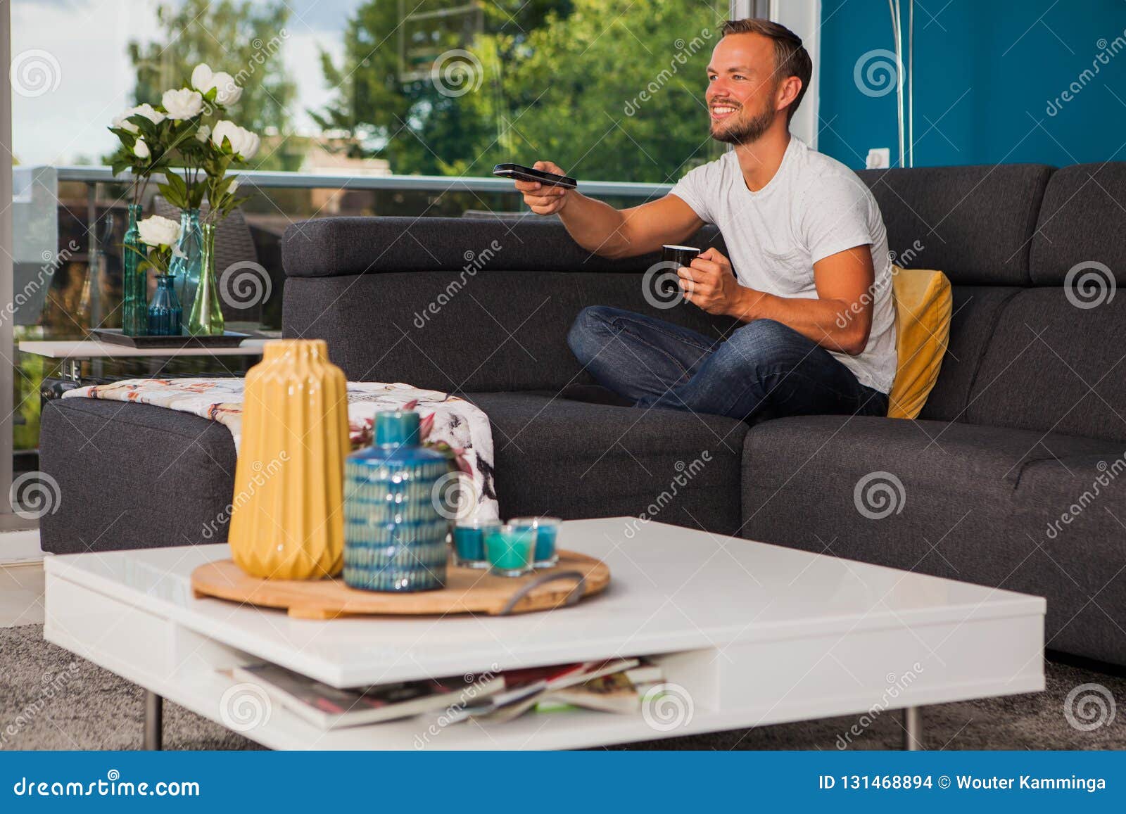 Young Man Using a Remote Control while Drinking Coffee on the Couch ...