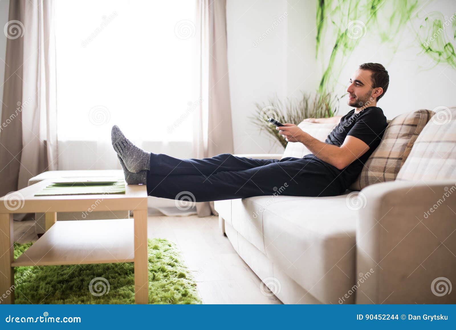 Young Man Using Remote Control while Sitting on Couch in Living Room ...