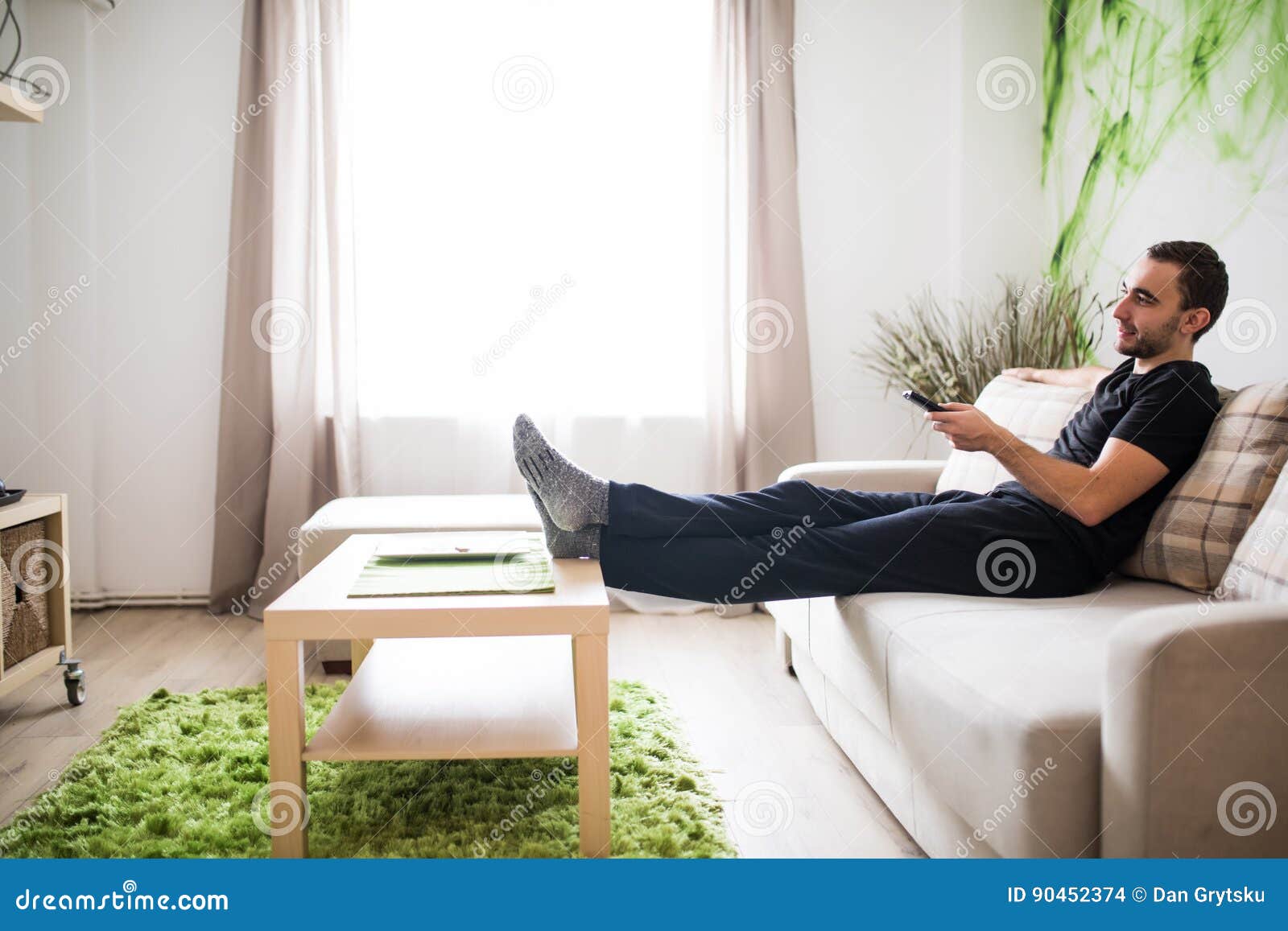 Young Man Using Remote Control while Sitting on Couch in Living Room ...