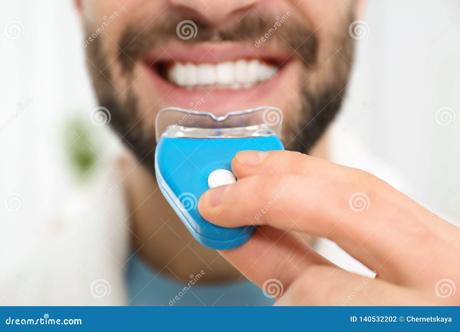 Young Man Using Teeth Whitening Device on Light Background Stock Photo ...