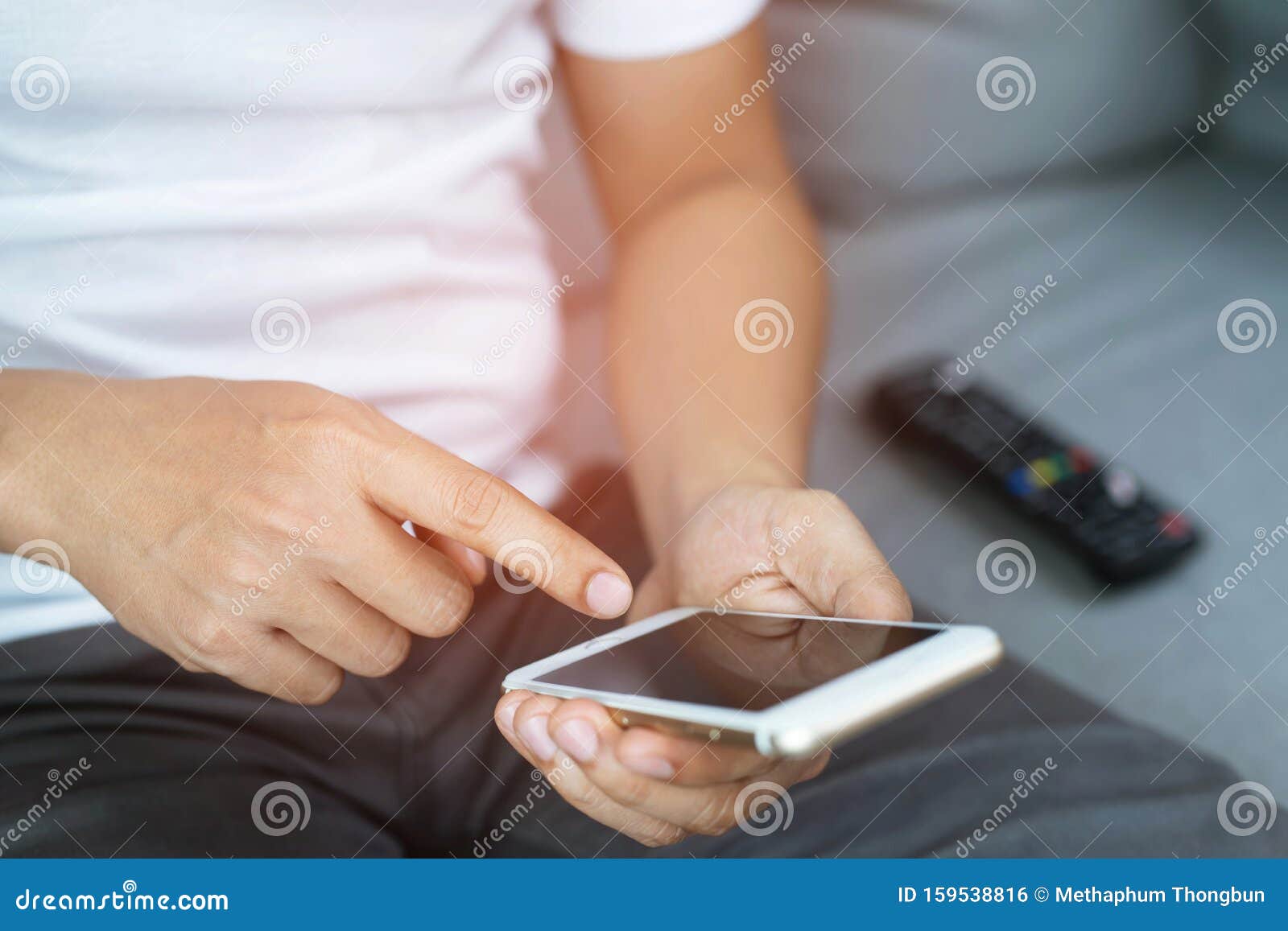 Young Man Using Television Remote Control and Mobile Smart Phone is ...