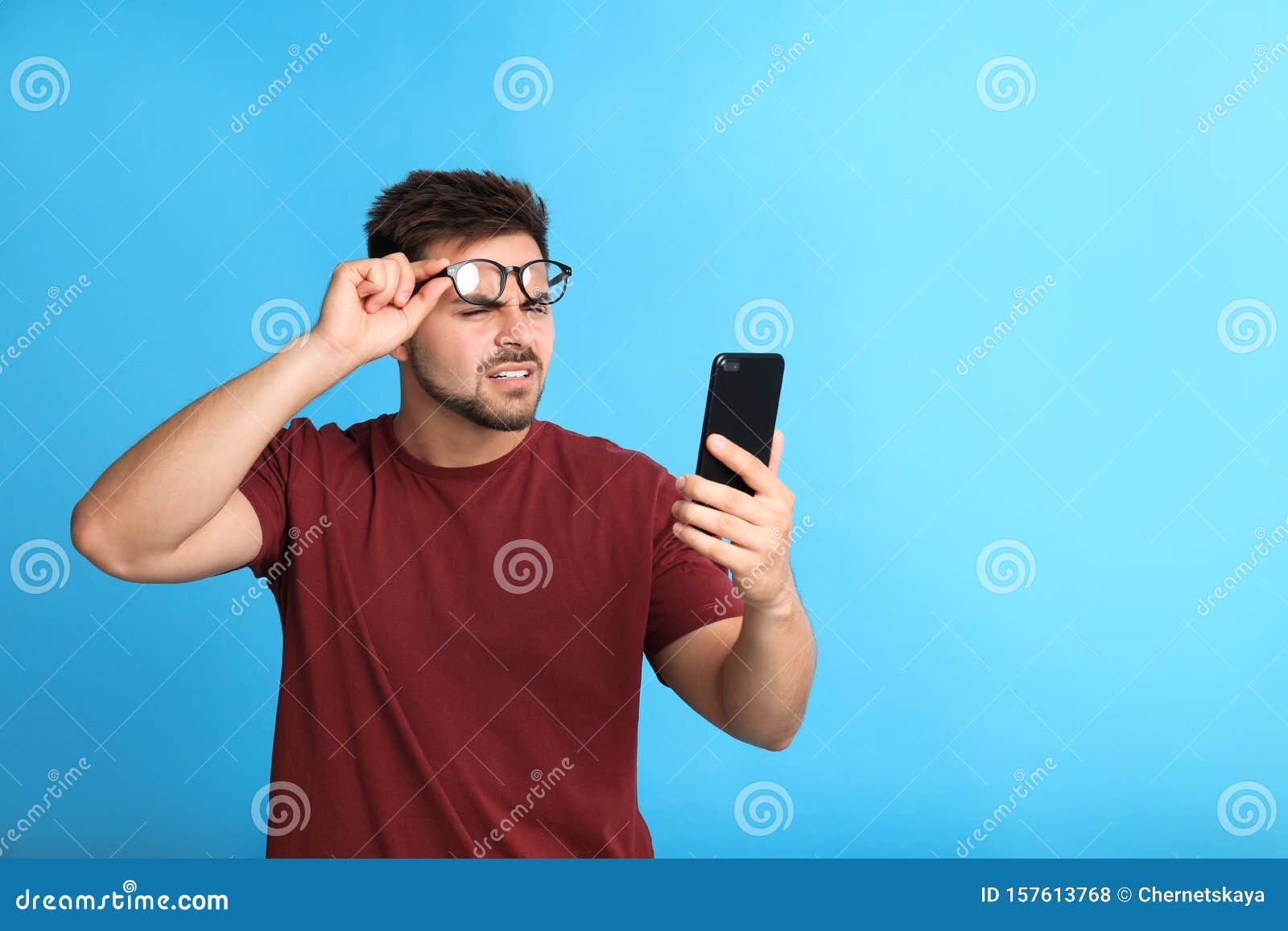 Young Man with Vision Problems Using Smartphone on Blue Background ...