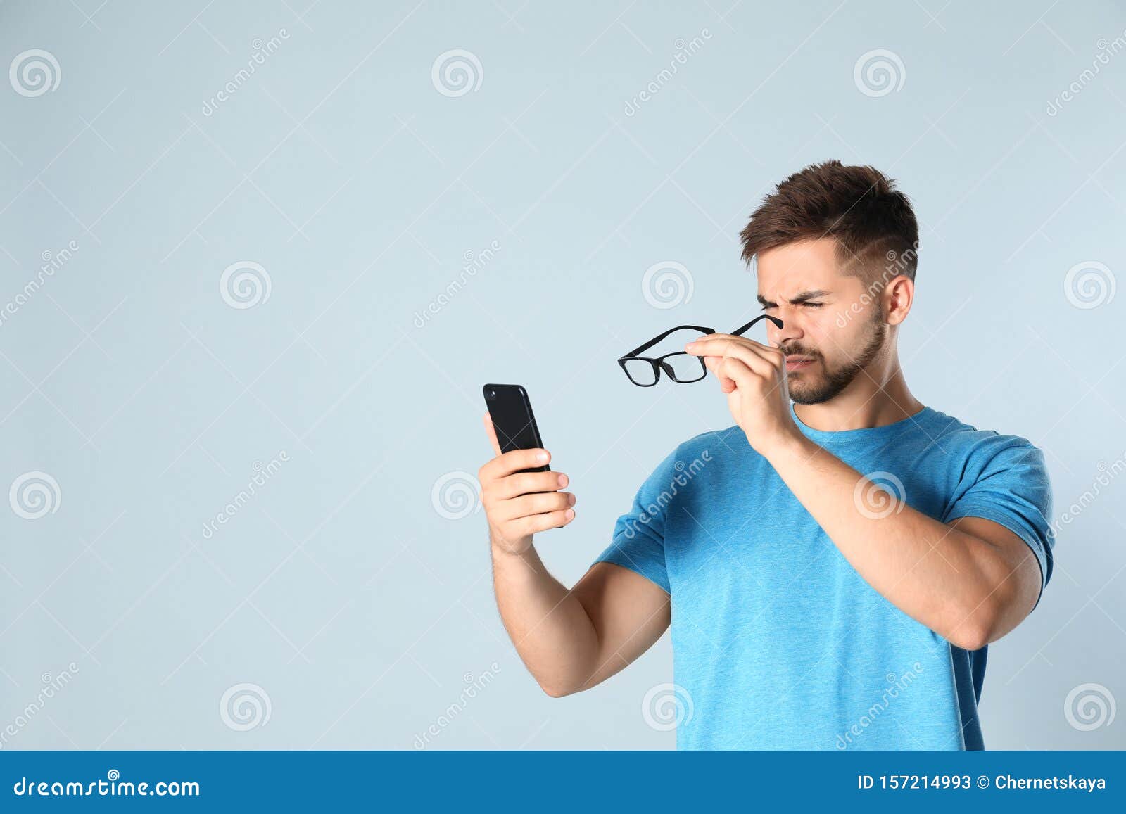 Young Man With Vision Problems Using Smartphone On Grey Background ...
