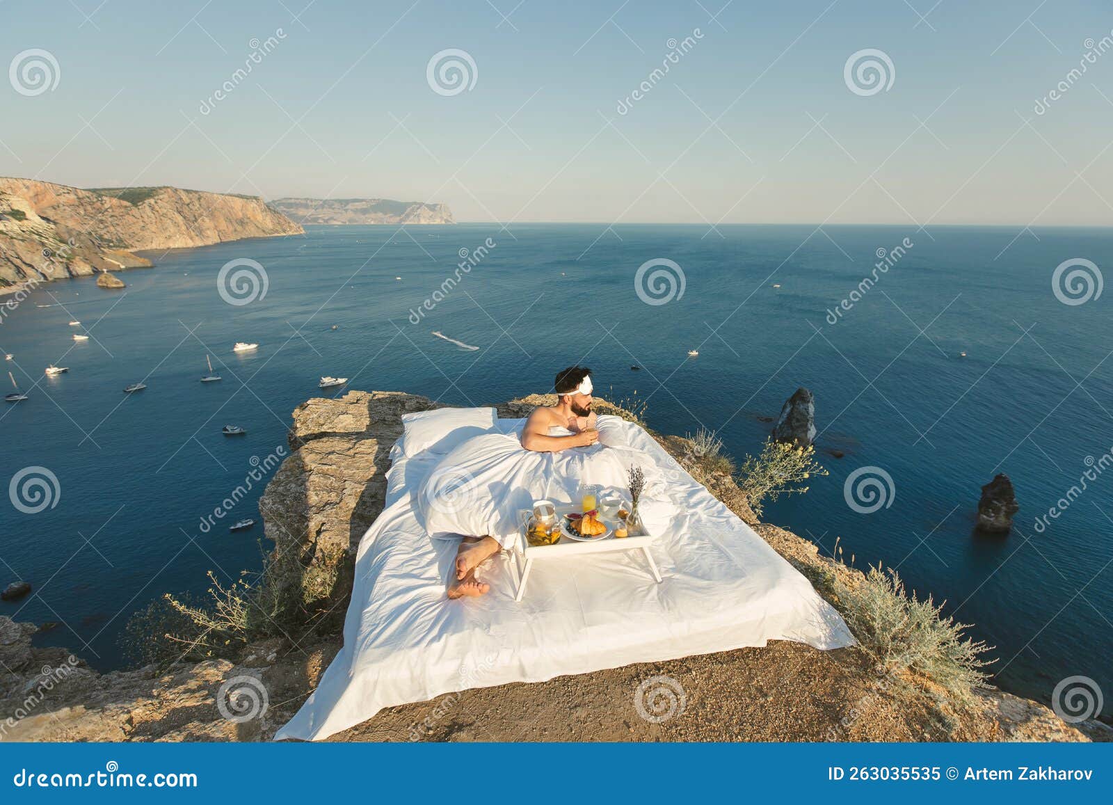 A Young Man Wakes Up Alone in a White Bed on a Cliff Overlooking the ...