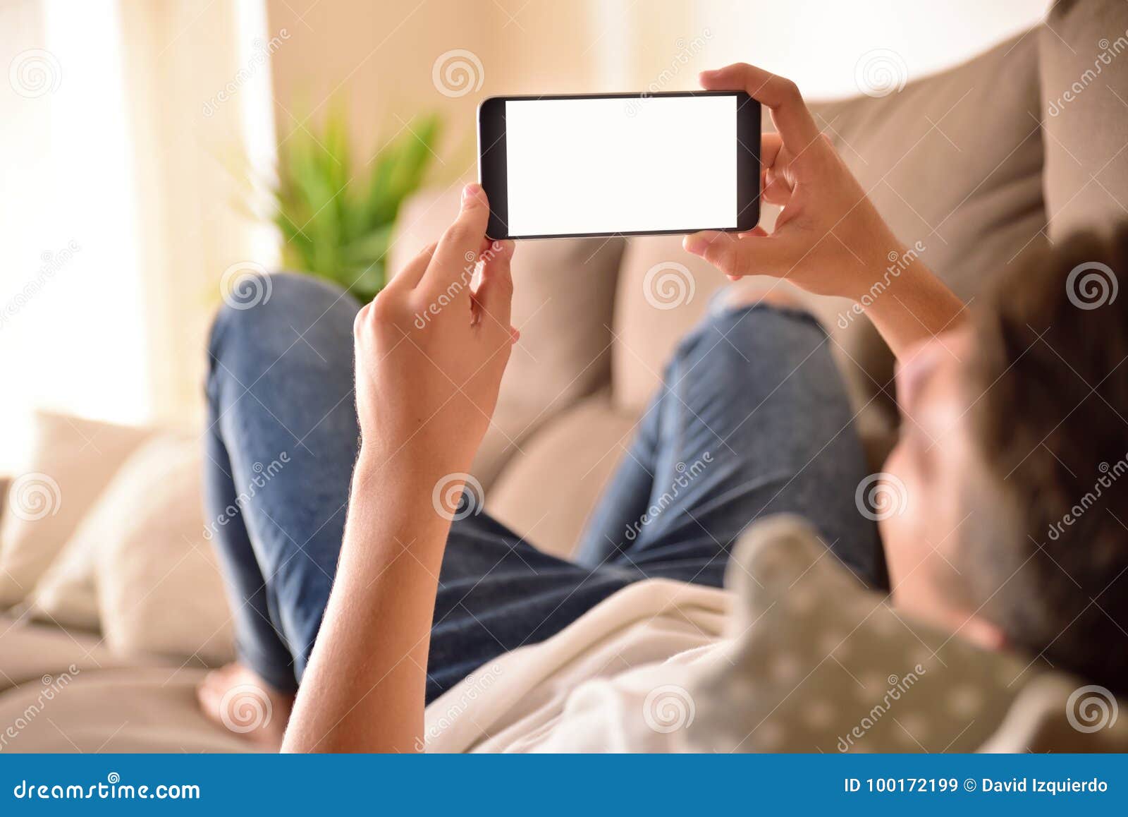 Young Man Watching Multimedia Content on a Smartphone Lying on a Stock ...