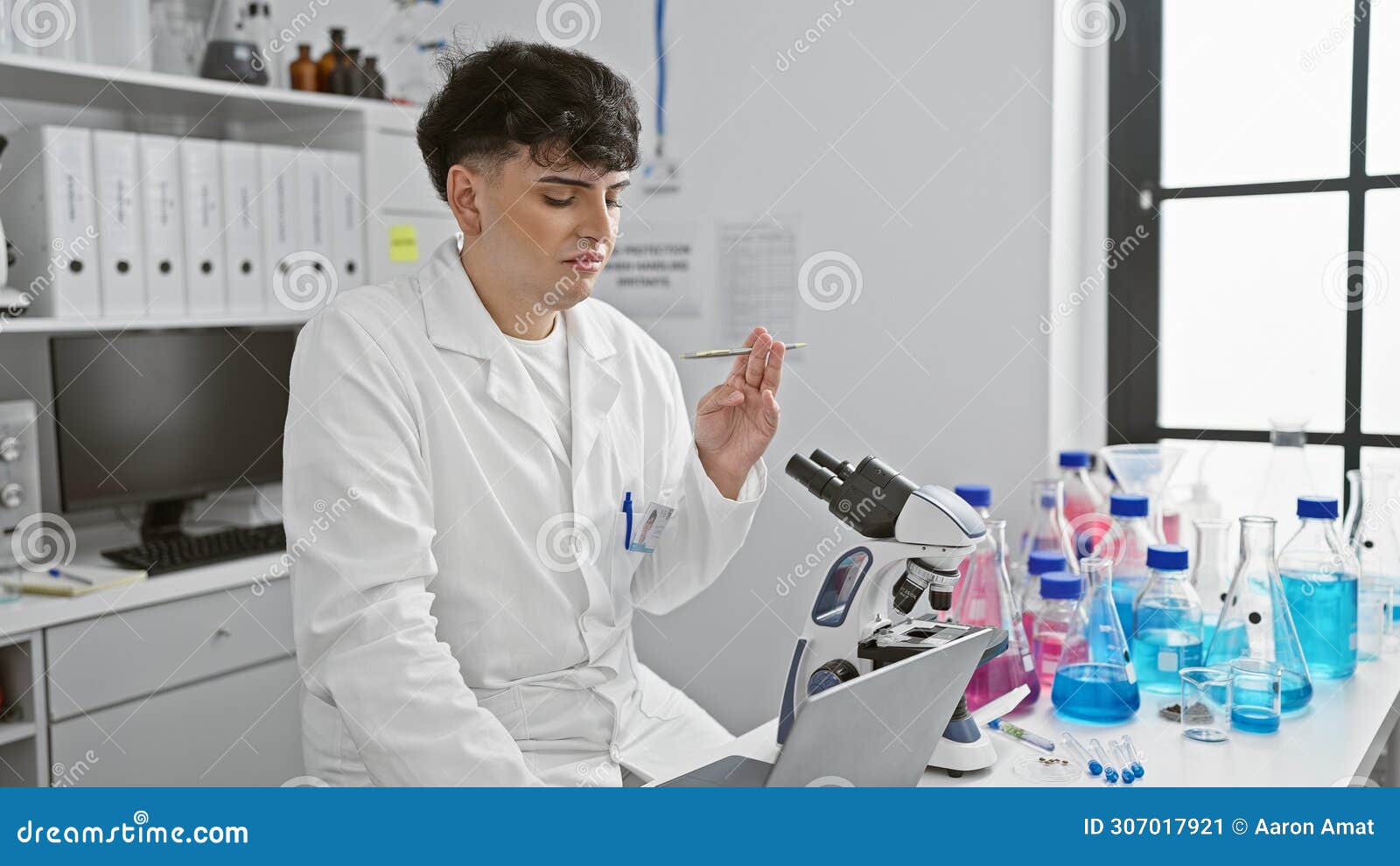 A Young Man in a White Lab Coat Examines a Pen while Working with a ...