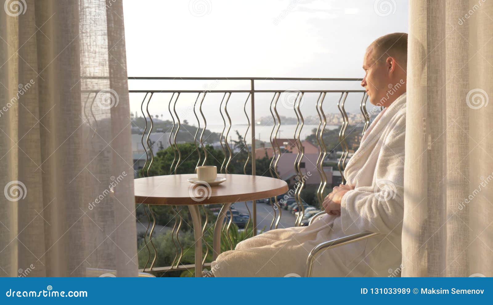 A Young Man in a White Robe Drinking Coffee on the Terrace. 4K Stock ...