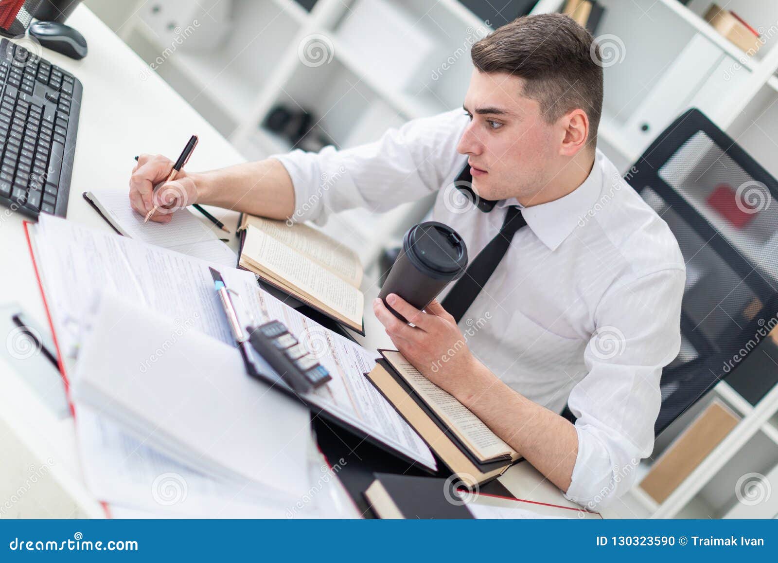 A Young Man Working at a Table in the Office with a Book, Documents and ...