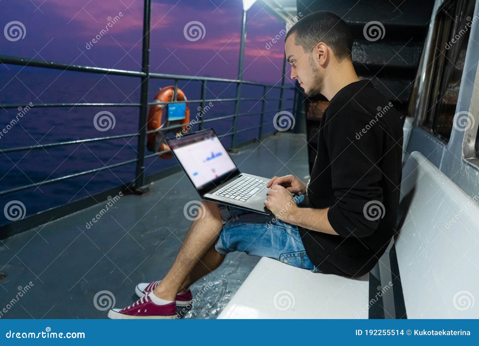 A Young Man Works on a Laptop on the Deck of a Ship. Remote Work Stock ...