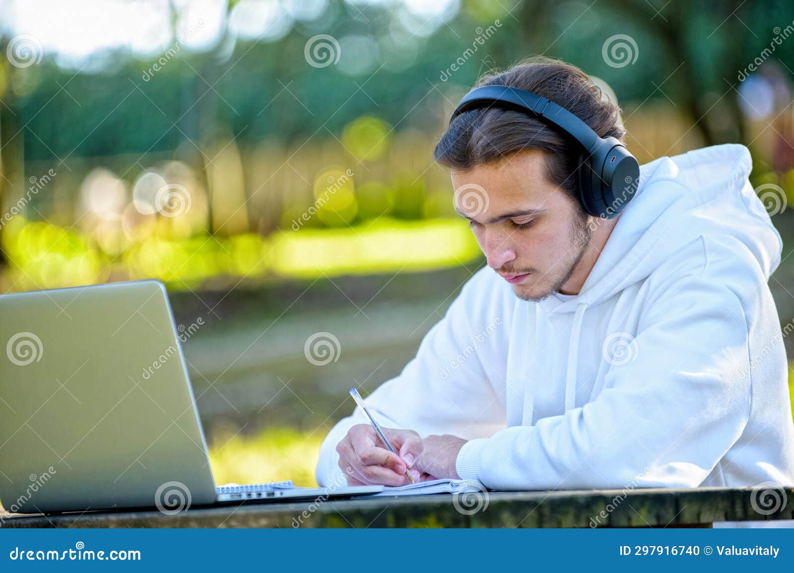 Young Man Writes with a Pen in a Notebook at a Table in the Park ...