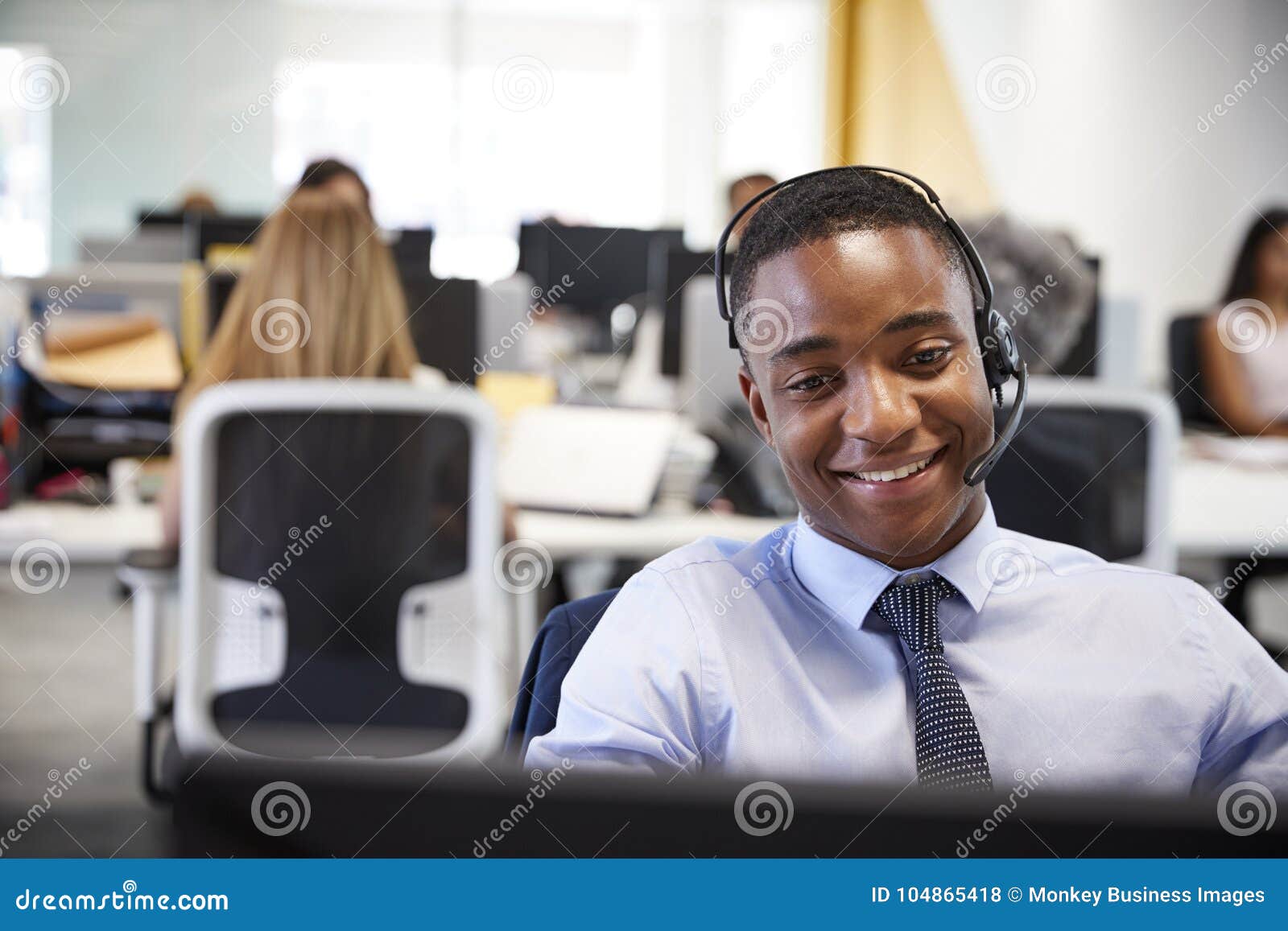 Young Man Working at Computer with Headset in Busy Office Stock Photo ...