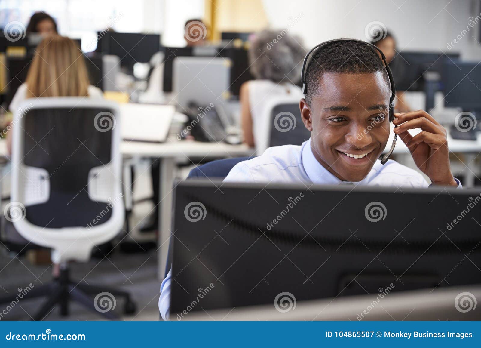 Young Man Working at Computer with Headset in Busy Office Stock Image ...