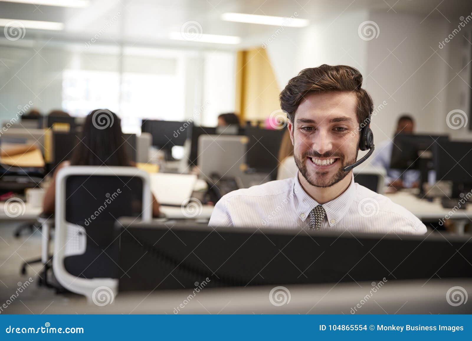 Young Man Working at Computer with Headset in Busy Office Stock Photo ...
