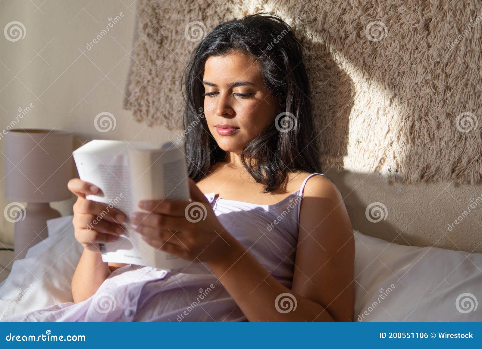 Young Middle Eastern Female Lying On Her Bed And Reading A Books Stock