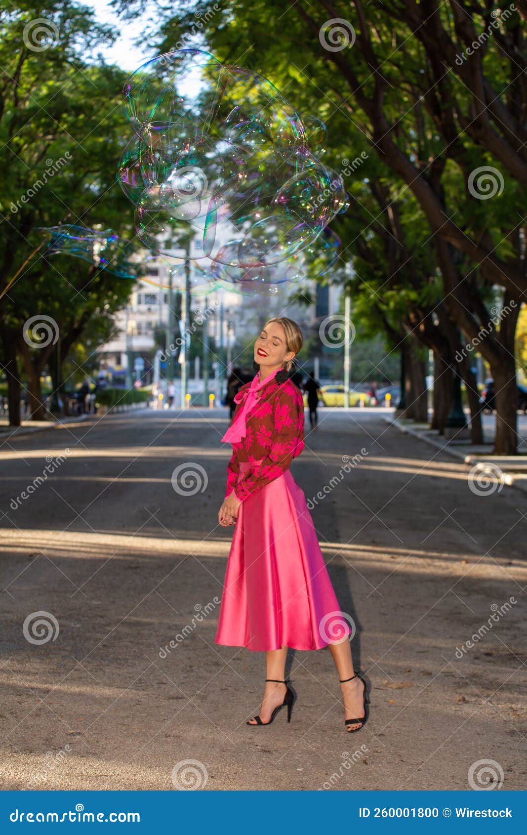 Young Model Posing Outside In Park In Long Pink Dress With Big Soap Bubbles Falling In