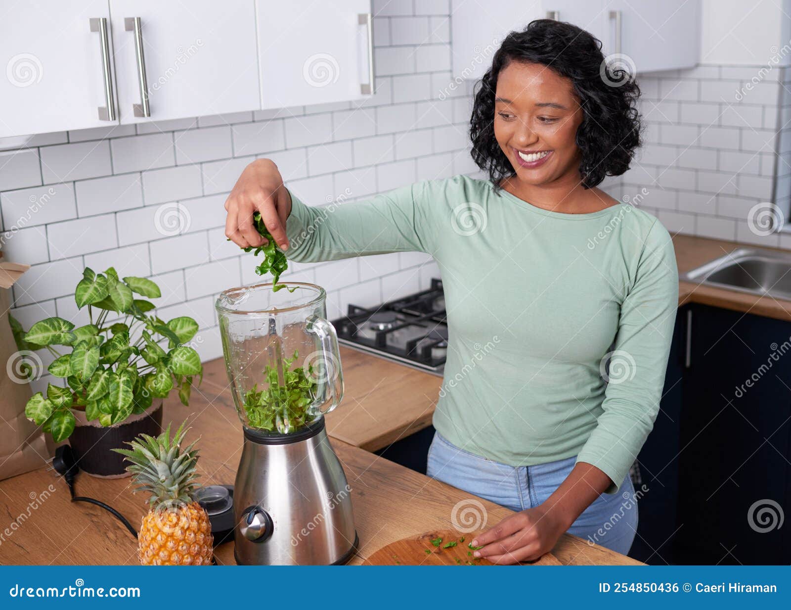 A Young Multi Ethnic Woman Puts Chopped Spinach Into A Blender To Make