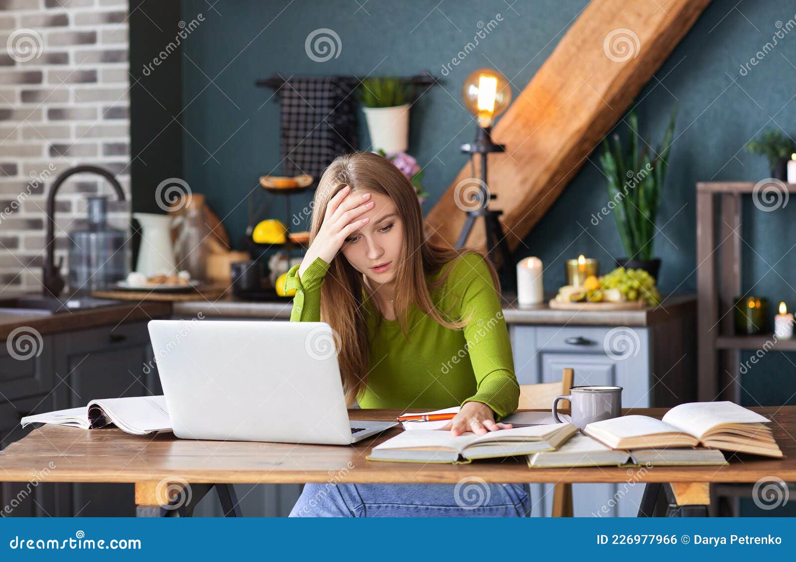 Young Pensive Woman Freelancer Sitting At Table At Home With Laptop