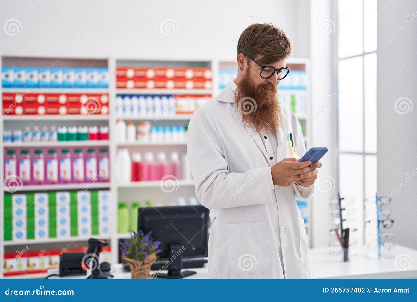 Young Redhead Man Pharmacist Using Smartphone Working at Pharmacy Stock ...