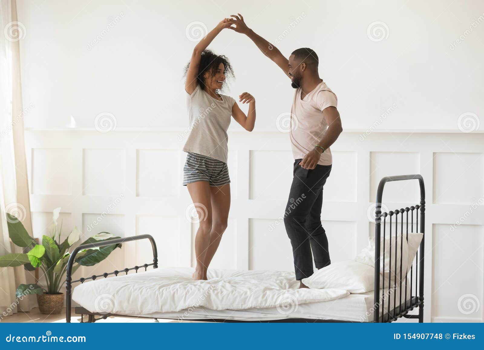 Young Romantic African American Couple Wearing Pajamas Dancing On Bed