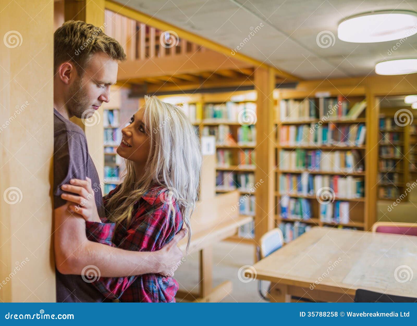 Young Romantic Couple with Bookshelf at Distance in Library Stock Photo ...