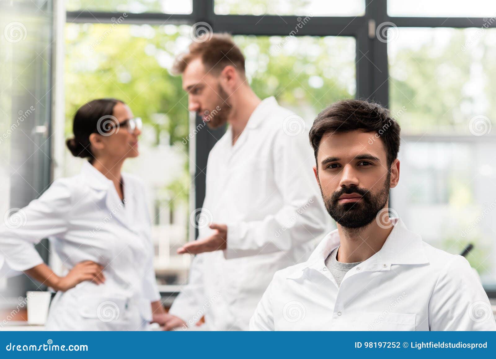 Young Scientist Looking at Camera while Colleagues Talking Behind Stock ...