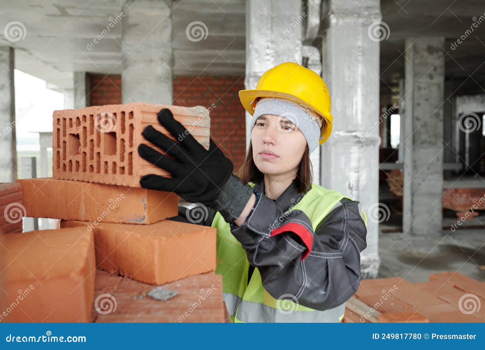 Young Serious Female Builder in Protective Helmet and Workear Taking ...