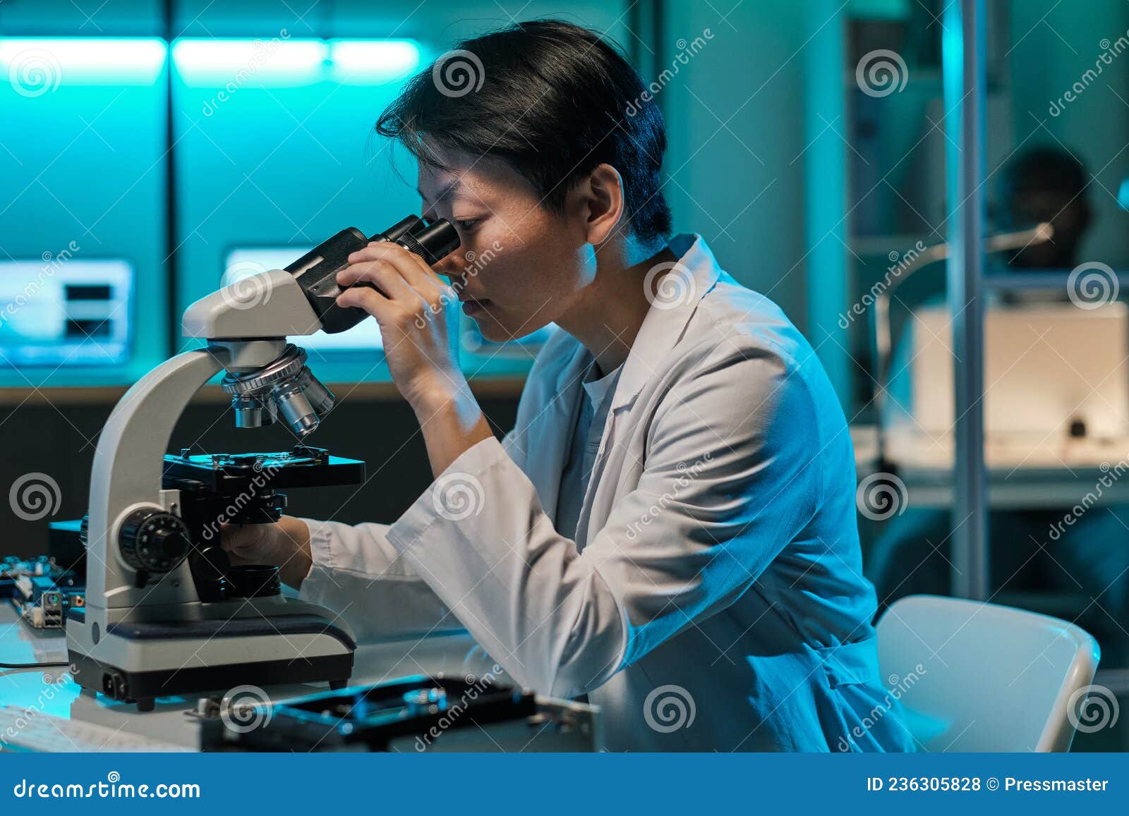 Young Serious Laboratory Worker Looking at Microchip in Microscope ...