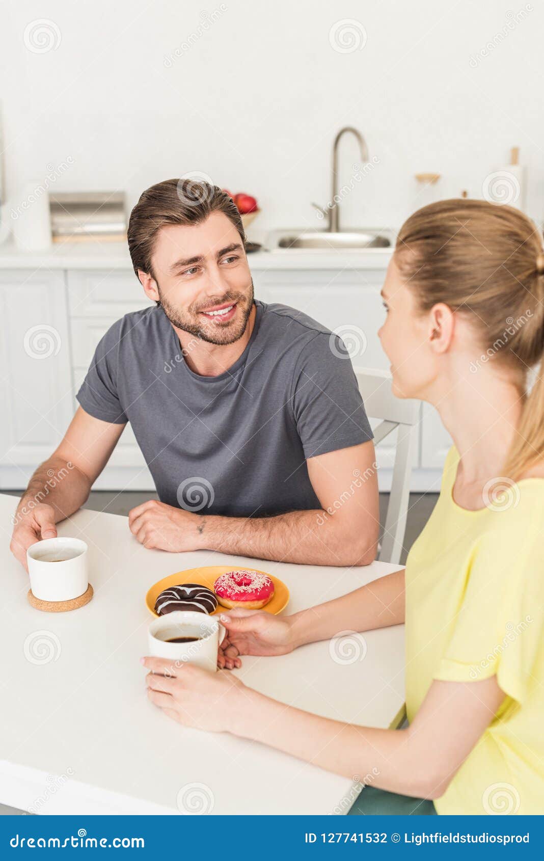 Young Smiling Couple Having Conversation at Kitchen Table with Donuts ...