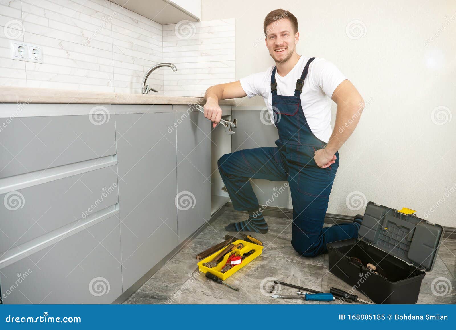 Young Smiling Man Plumber in Uniform Fixing the Sink with Adjustable ...