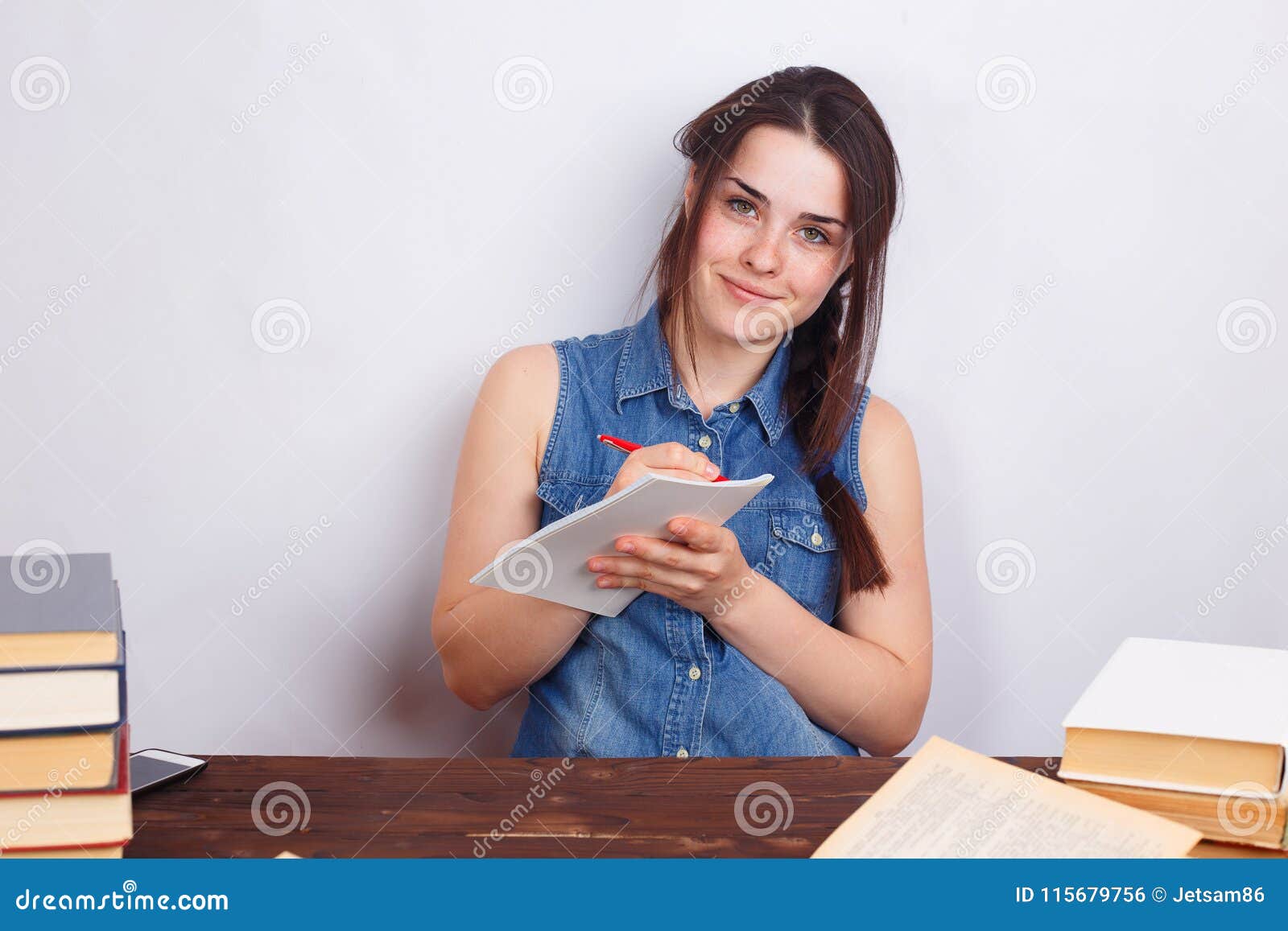 Young Smiling Student Woman Sitting at the Desk, Writing Down a Stock ... Young Smiling Student Woman Sitting at the Desk, Writing Down a Stock ...
