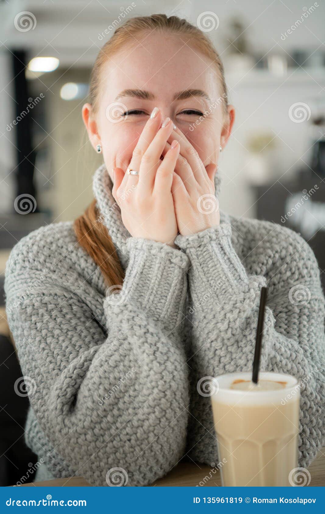 Young Smiling Woman Sitting In Cafe At Table Smiling With Hands On Her