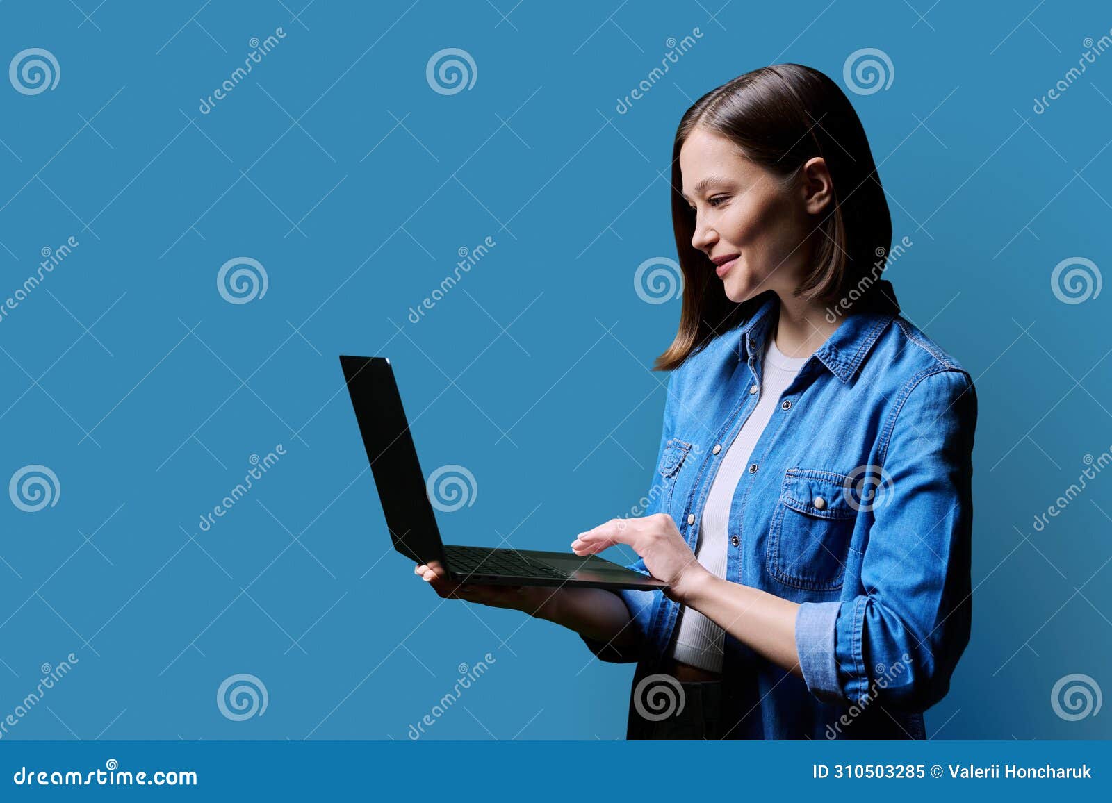 Young Smiling Woman Using Laptop, Profile View on Blue Background Stock ...