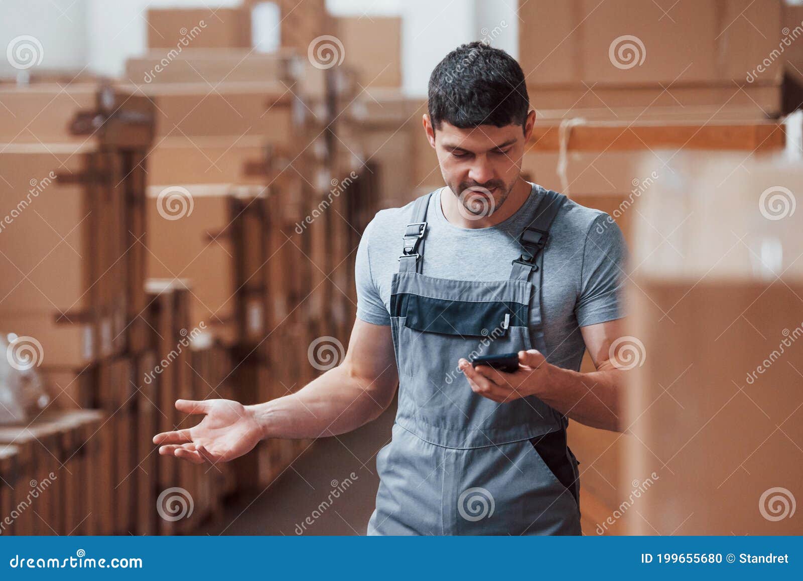 Young Storage Worker in Uniform Stands and Uses His Phone Stock Photo ...