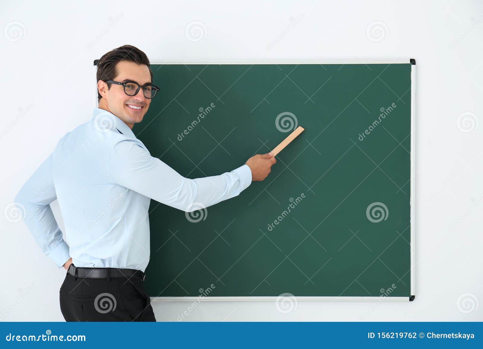 Young Teacher with Ruler Near Blank Chalkboard in Classroom. Space for ...