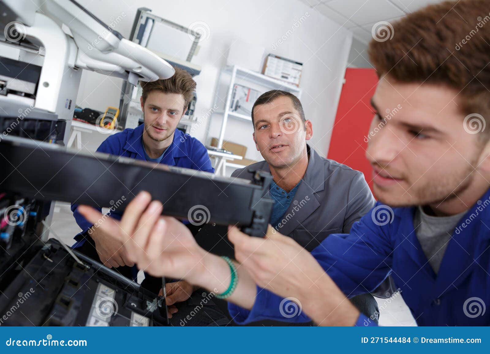 Young Technician Working on Photocopier Being Supervised by Colleagues ...